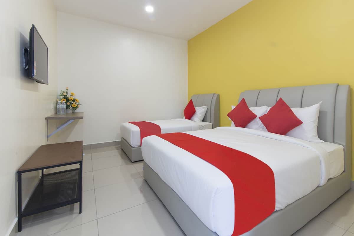 Quarto de hotel com duas camas, televisão, uma mesinha com um vaso de flores e uma parede amarela.