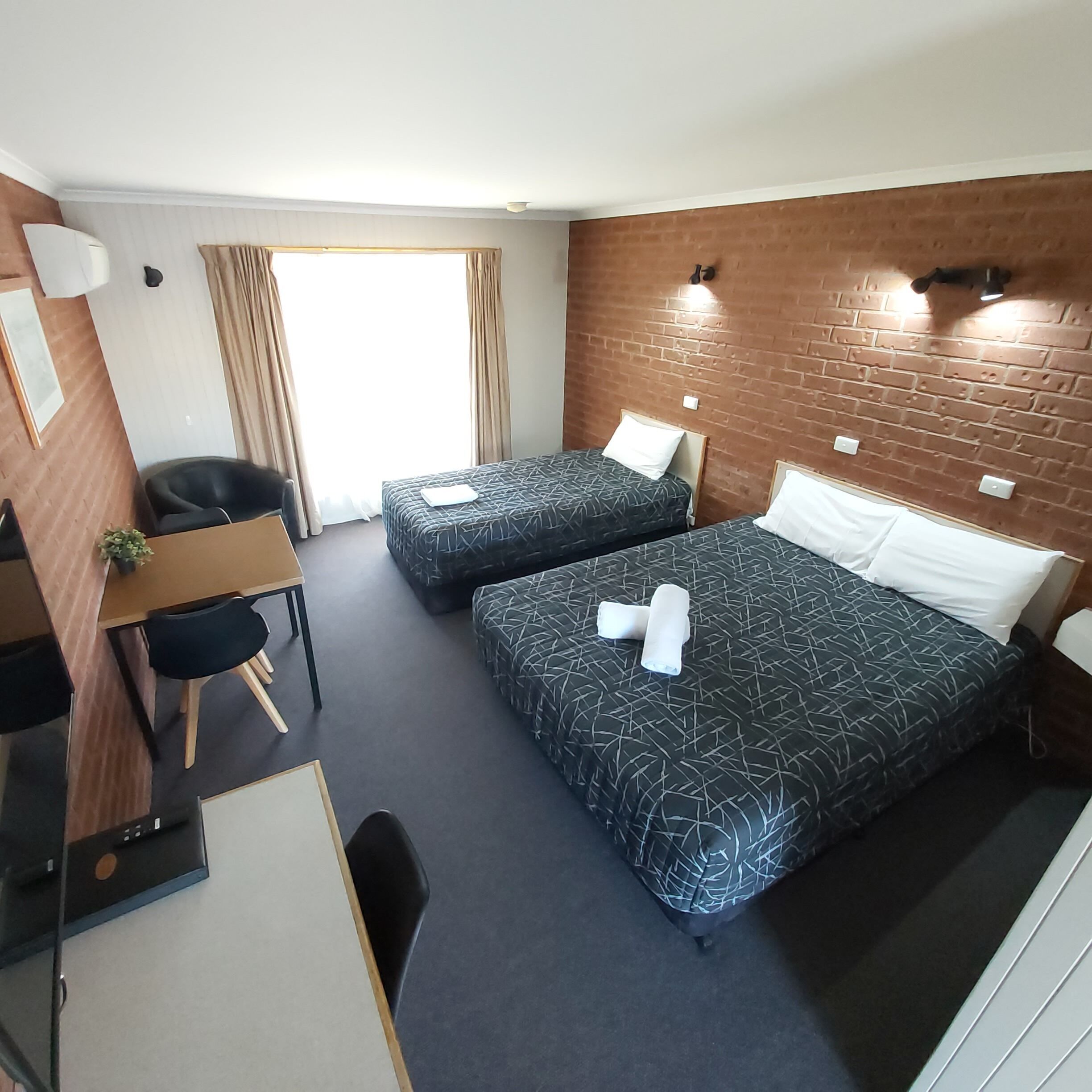 Quarto de hotel com duas camas, uma escrivaninha, uma cadeira e uma janela com cortinas.