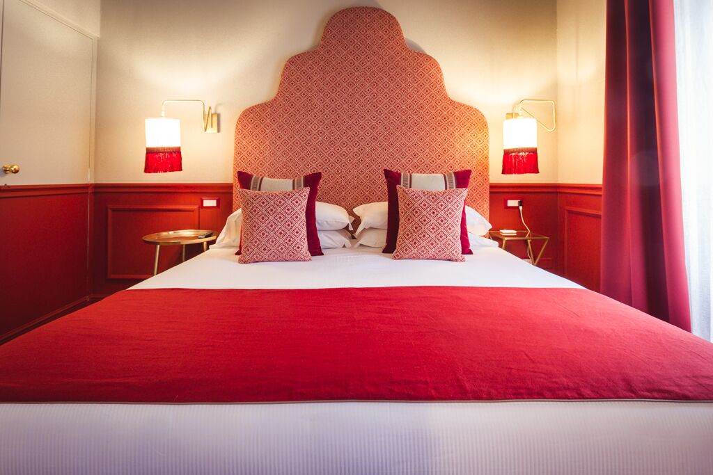 Quarto de hotel com uma cama grande, duas mesas de cabeceira e uma parede vermelha de destaque.