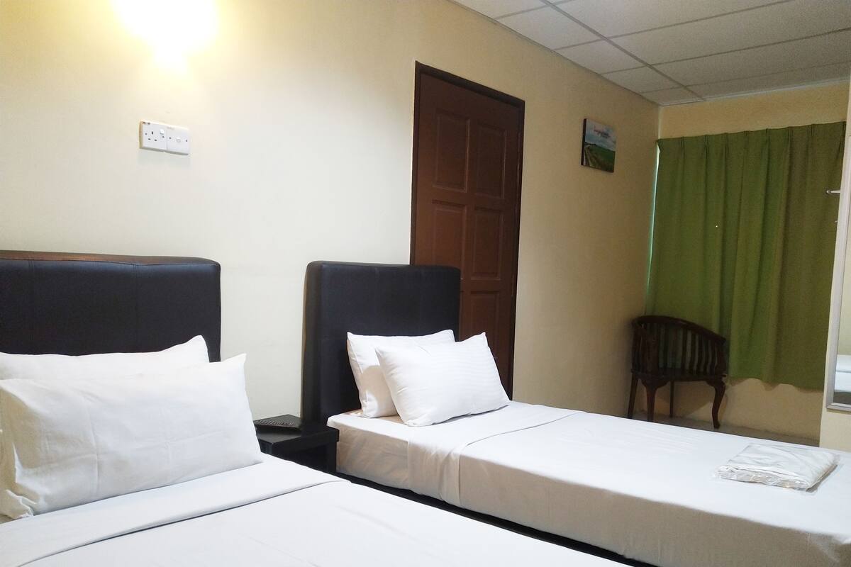 Duas camas de solteiro com roupa de cama branca e cabeceiras escuras em um quarto com porta de madeira e cortina verde.