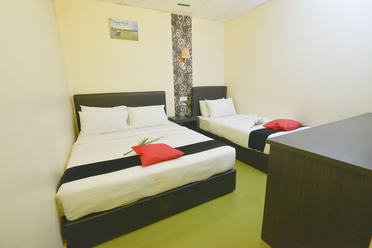 Quarto de hotel com duas camas, uma mesa de escritório e parede estampada.
