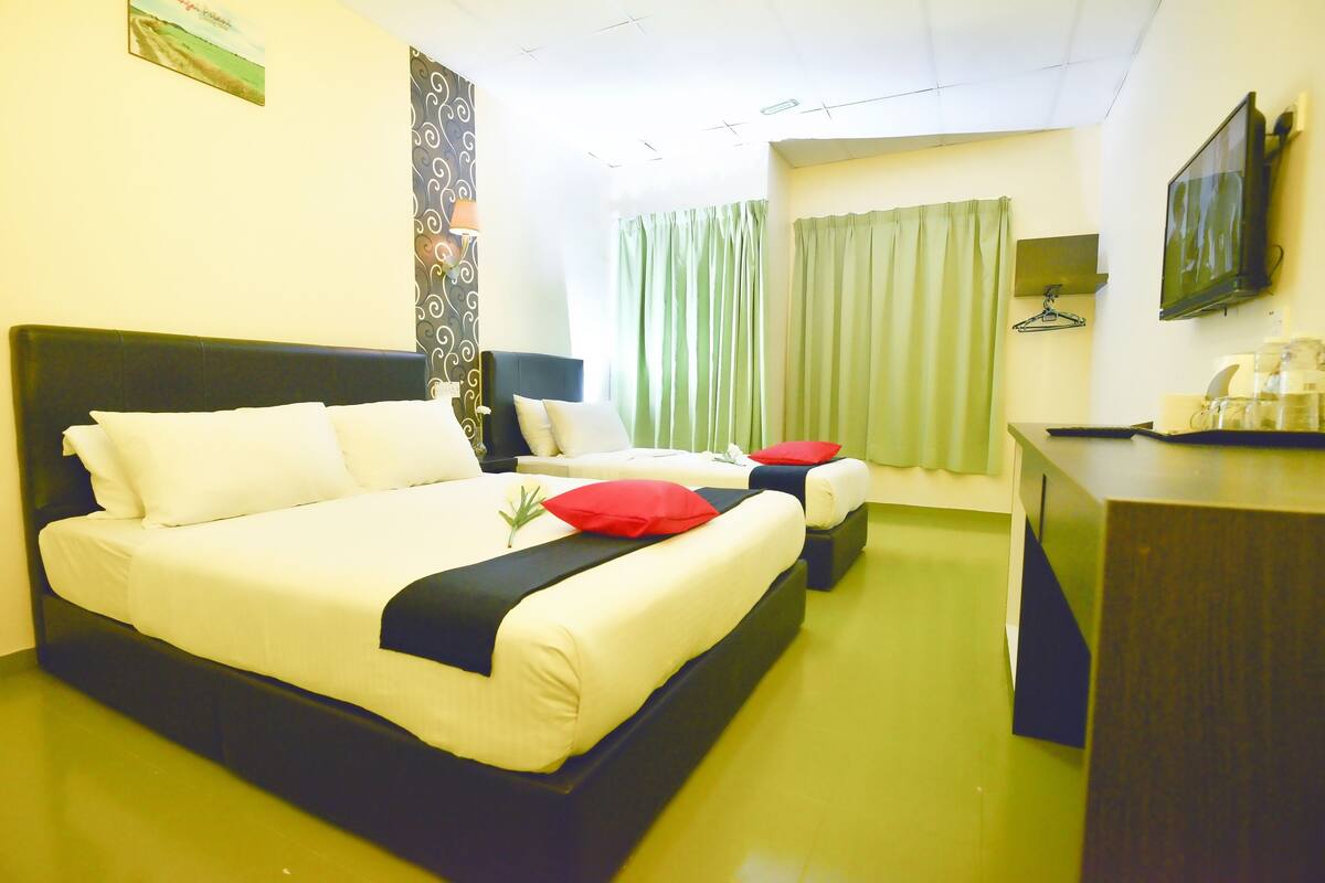 Quarto de hotel com uma cama grande, duas mesas de cabeceira, uma escrivaninha e uma televisão.