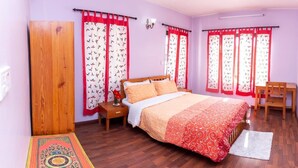 Quarto com cama de madeira, cortinas estampadas em vermelho e branco, mesa de cabeceira de madeira, uma cadeira e um tapete pequeno.