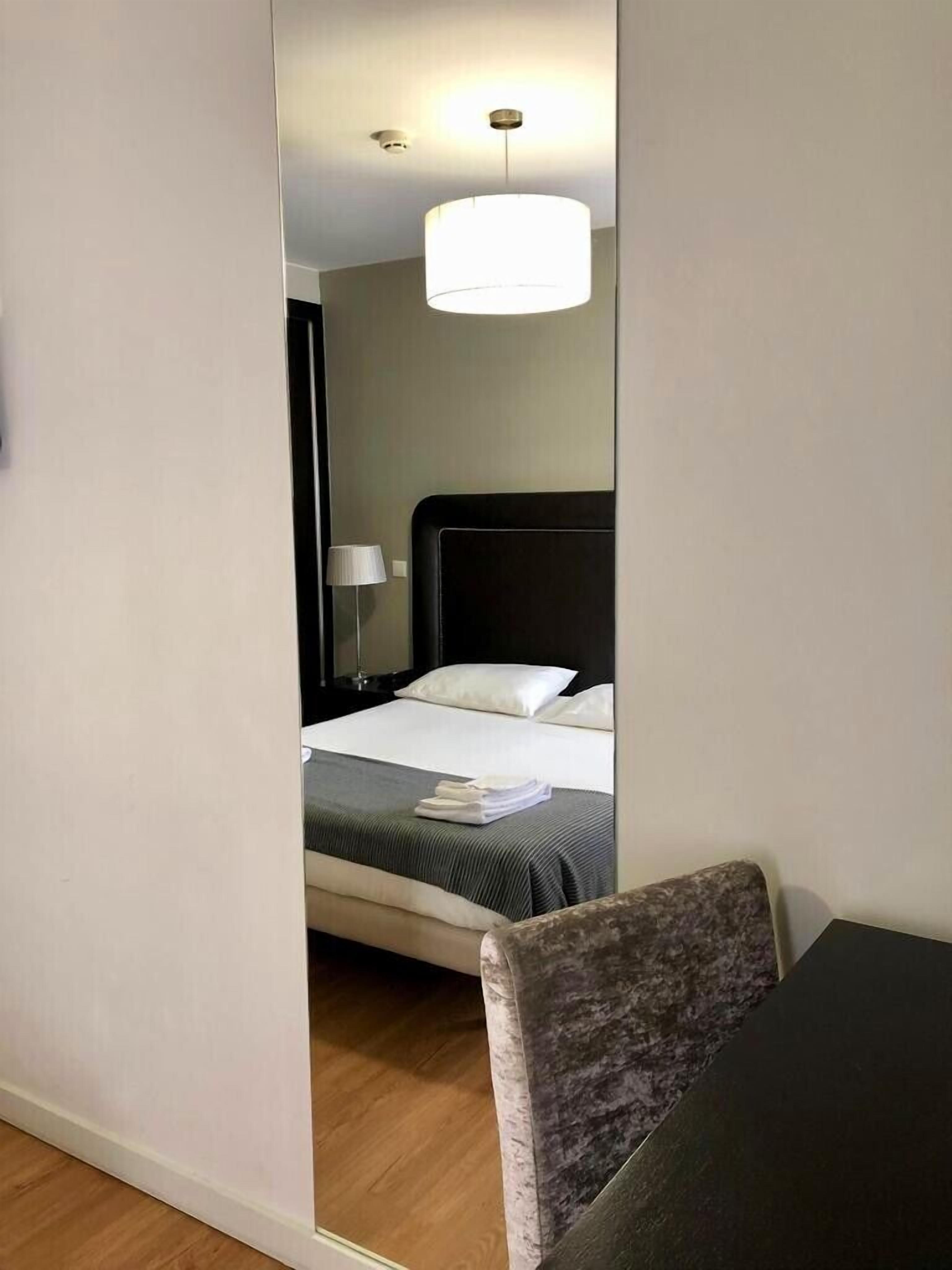 Quarto de hotel com cama, mesa de cabeceira, luminária e mesa de jantar.