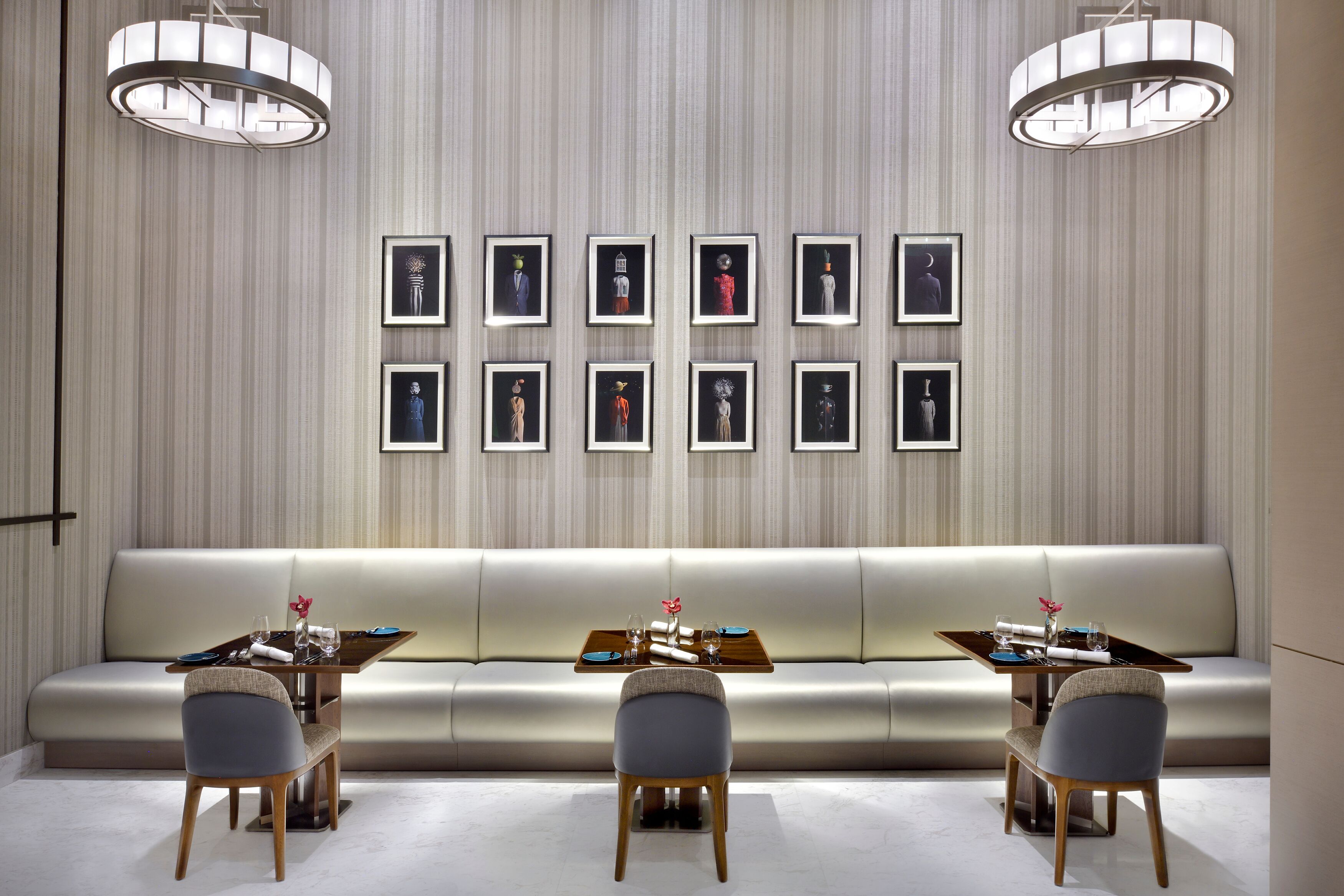 Quarto de hotel moderno com um sofá grande, duas mesas de jantar e quadros na parede.