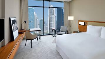 Quarto de hotel com uma cama grande, uma escrivaninha com cadeira, televisão e vista para arranha-céus da cidade.