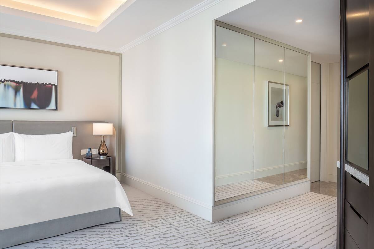 Quarto de hotel moderno com uma cama grande, abajur, box de vidro para o chuveiro e um quadro na parede.