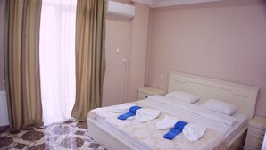 Quarto de hotel com cama, mesa de cabeceira, cômoda e janela com cortinas.