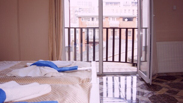 Quarto de hotel com cama, janela com vista para edifícios e varanda com corrimão.