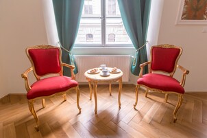 Duas cadeiras ornamentadas com estofamento vermelho e detalhes dourados, dispostas em torno de uma pequena mesa redonda com um bule e xícaras.