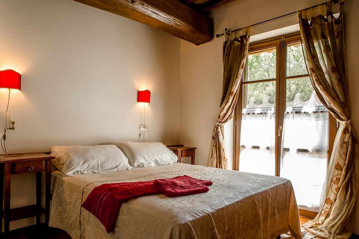 Quarto com cama grande, duas mesas de cabeceira, um criado-mudo e janela com cortinas.