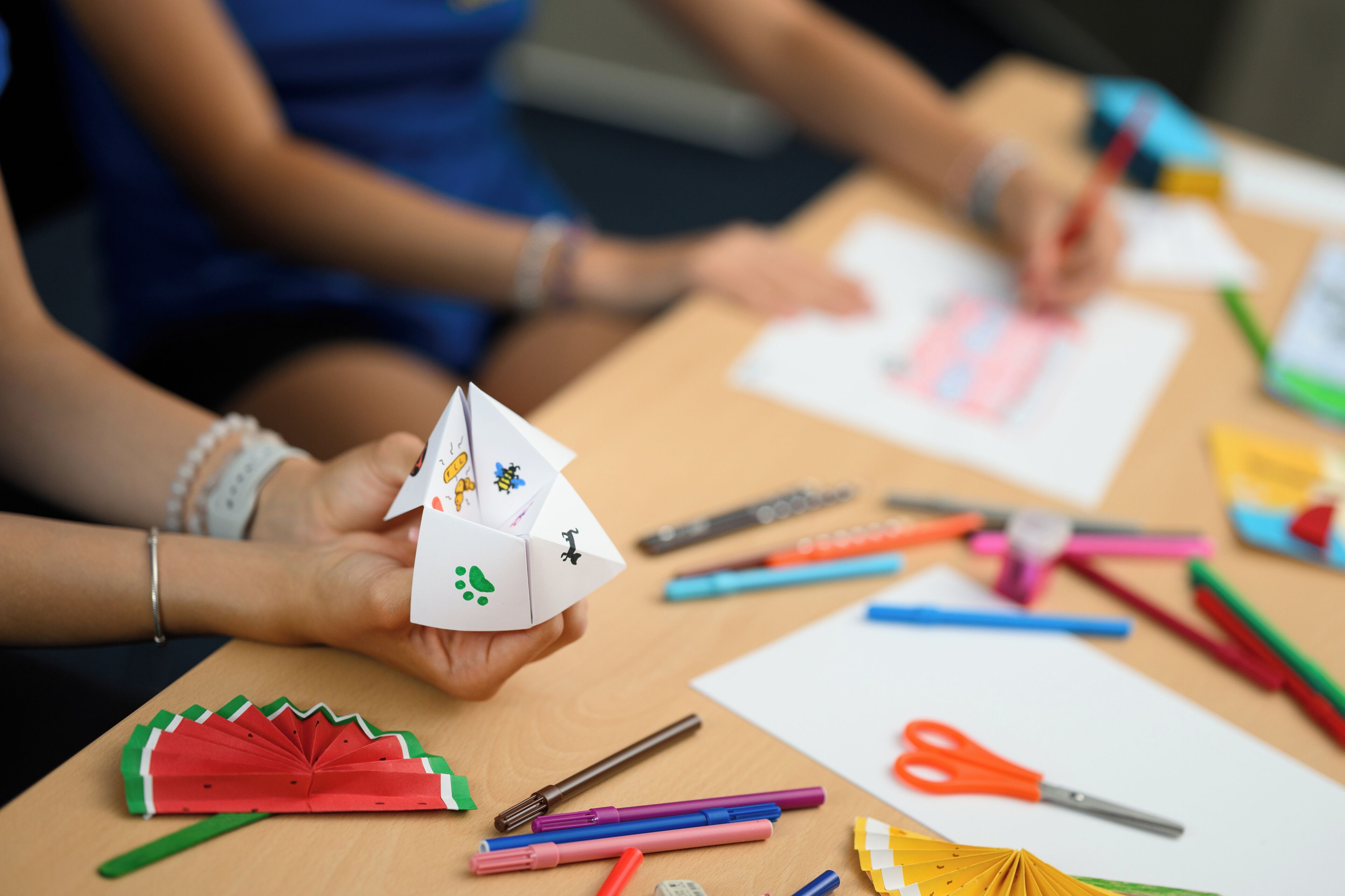 Uma pessoa segurando uma criação de papel, com diversos materiais de papelaria sobre uma mesa.