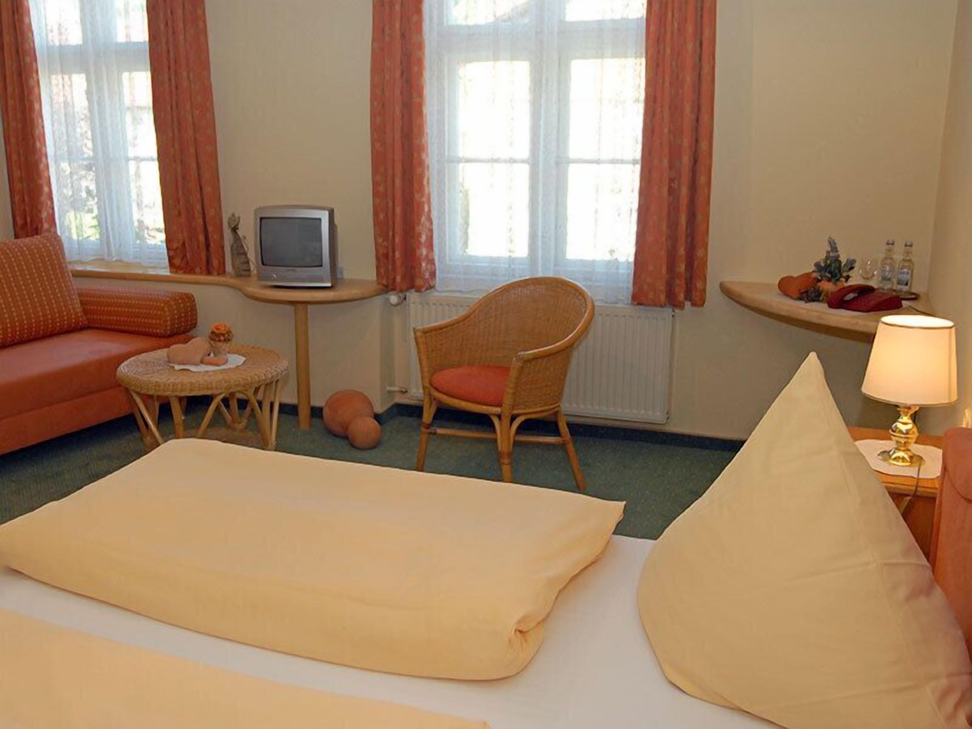 Quarto de hotel com uma cama, uma cadeira, uma mesa pequena com uma televisão e um abajur.