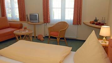 Quarto de hotel com uma cama, uma cadeira, uma mesa pequena com uma televisão e um abajur.