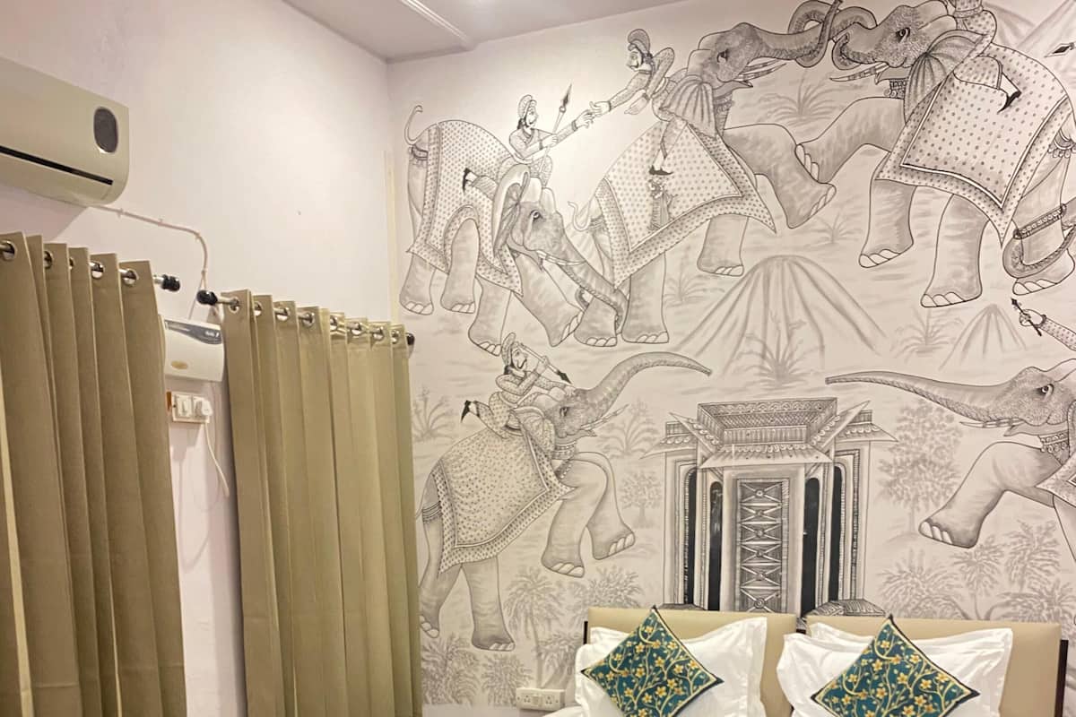 Quarto de hotel com cama, cortinas, uma cadeira e um mural de elefantes na parede.