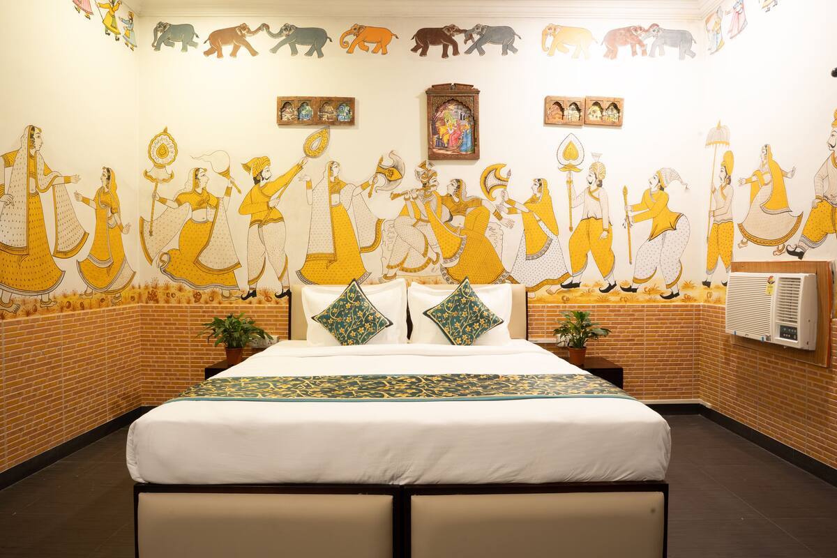 Quarto de hotel com uma cama grande, parede com padrão de tijolos e arte tradicional retratando dançarinos.