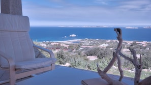 Uma área de estar externa com assentos brancos e vista para o mar e terra ao longe.