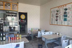Interior de restaurante com quadro de cardápio, mesas, cadeiras e balcão com acompanhamentos.