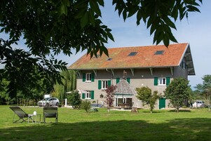 Uma casa de dois andares com telhado inclinado, persianas verdes e um pequeno jardim com um gazebo.
