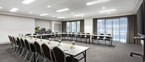 Uma sala de conferências com uma mesa comprida, cadeiras e uma tela de projeção.