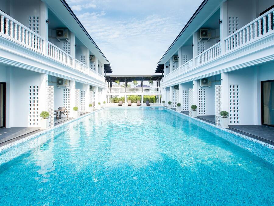 Piscina com superfície de água azul cristalina, rodeada por edifícios brancos com varandas e aparelhos de ar condicionado.