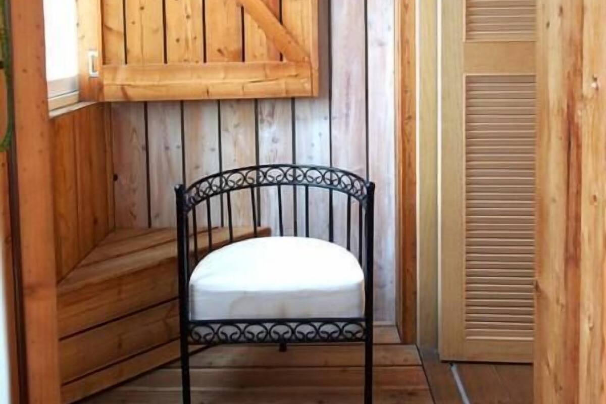 Interior de uma cabana de madeira com um banco, uma porta de madeira e uma janela.