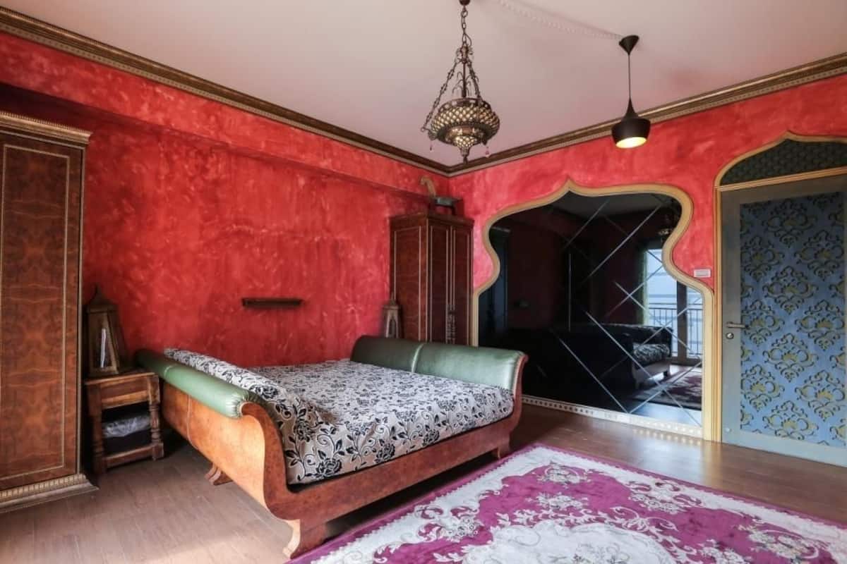 Um quarto com uma cama, um armário de madeira, um candeeiro pendente e um tapete estampado.