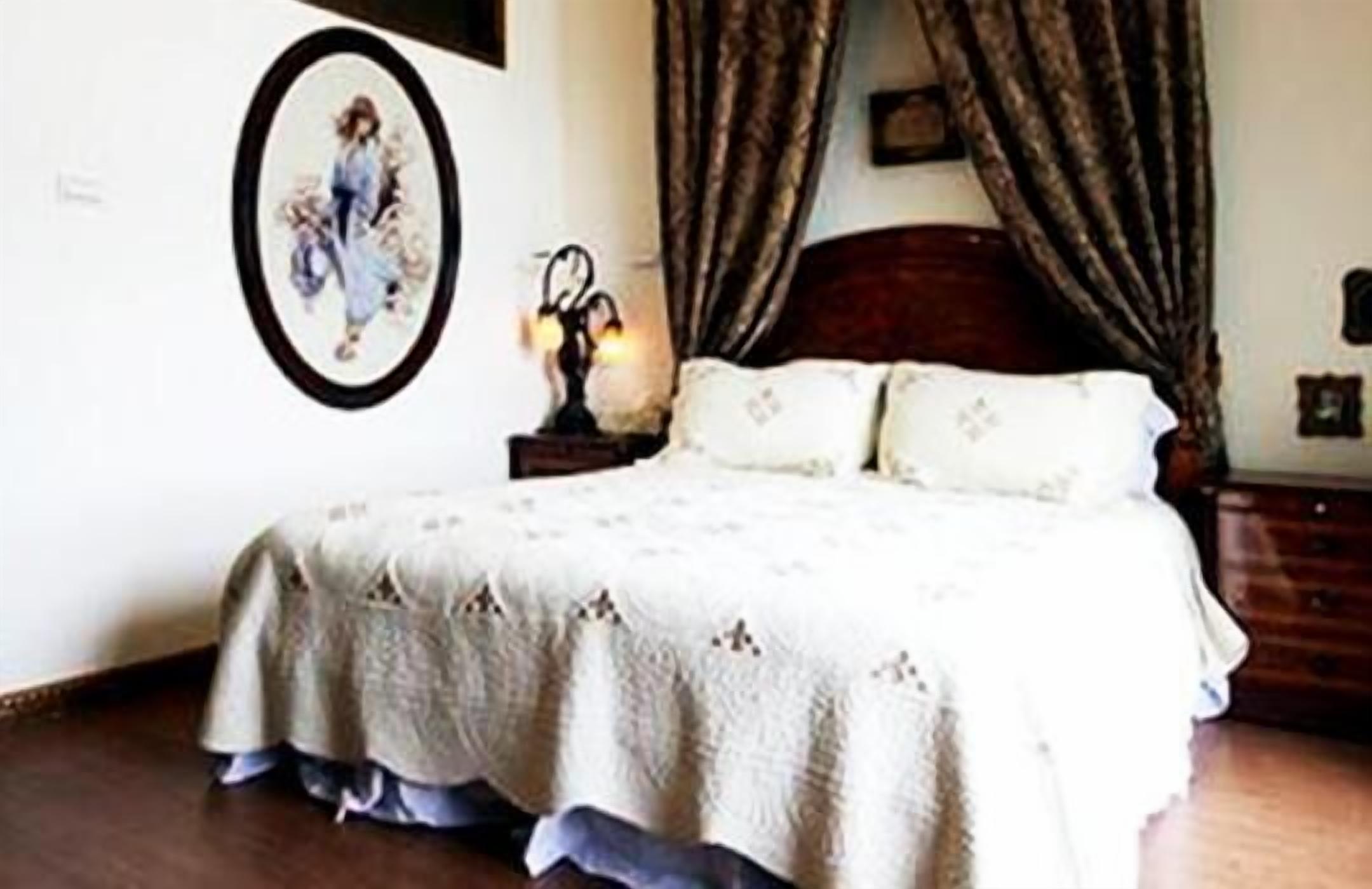 Quarto com cama, mesa de cabeceira, abajur e um quadro na parede.