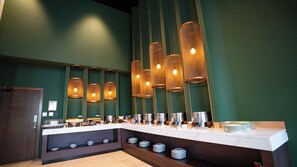 Uma área de buffet com um balcão branco, luminárias de vime pendentes e uma parede verde.