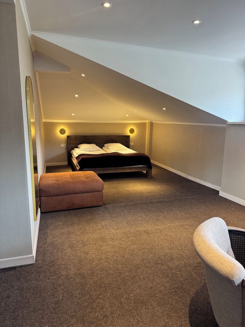Um quarto com uma cama, um banquinho e uma cadeira.