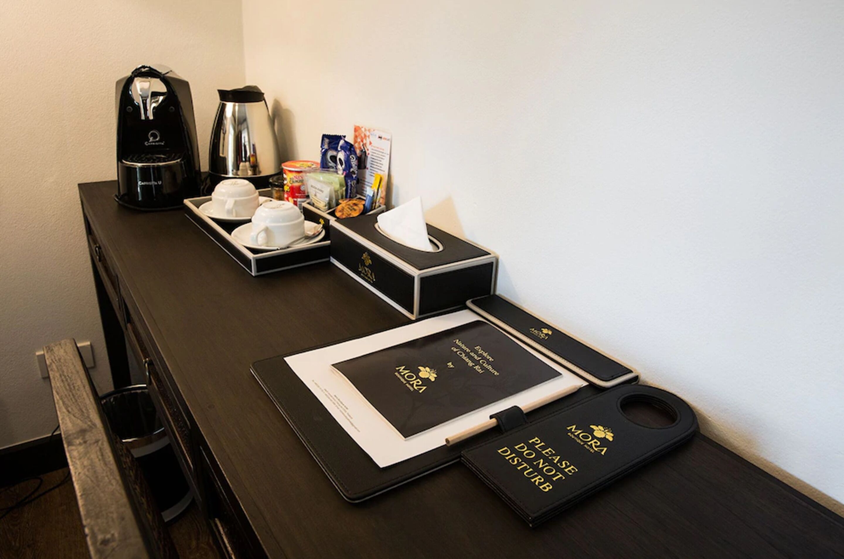 Quarto de hotel bem organizado, com cafeteira, chá, lenços de papel, bloco de notas e carteira com placa 'Não Perturbe'.