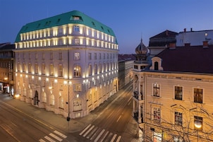 Um edifício histórico com telhado verde e vários andares, com grandes janelas e uma entrada de esquina imponente.