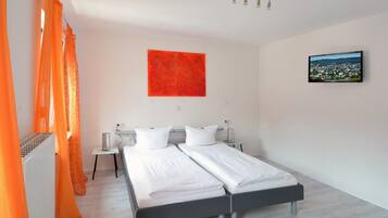 Quarto de hotel moderno com duas camas de solteiro, uma janela grande com cortinas laranja, uma televisão de tela plana na parede e um quadro abstrato vermelho acima das camas.