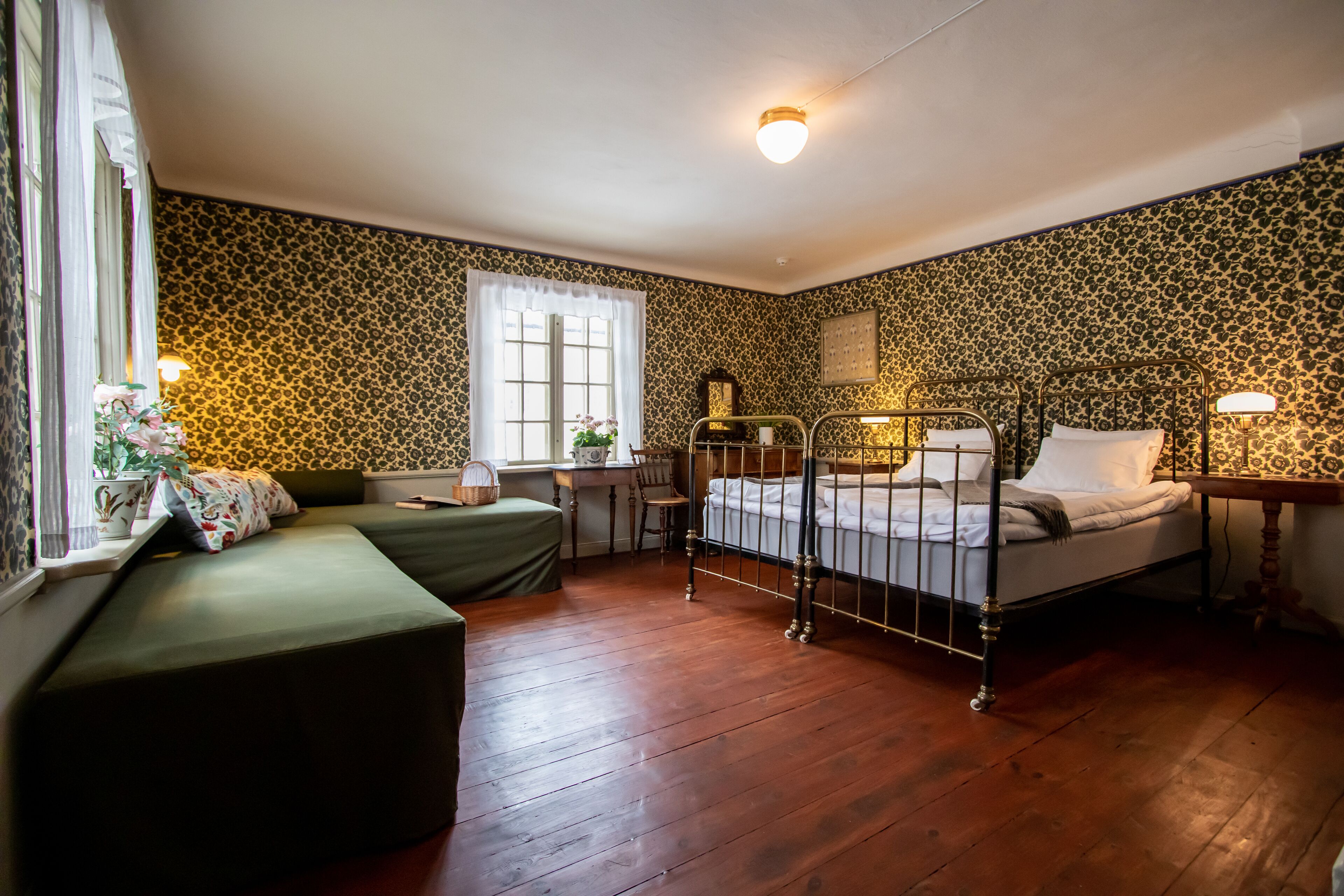 Quarto com uma cama, um banco, uma mesa e uma janela com cortinas.