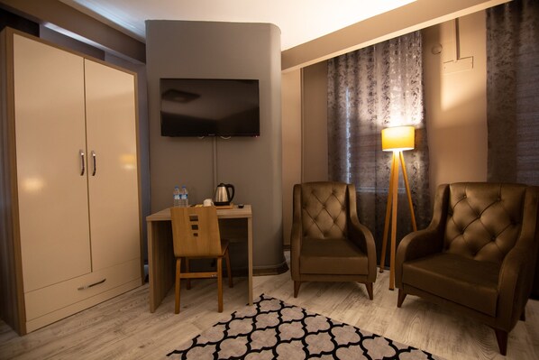 Quarto de hotel com uma escrivaninha, duas poltronas, uma televisão e um abajur.