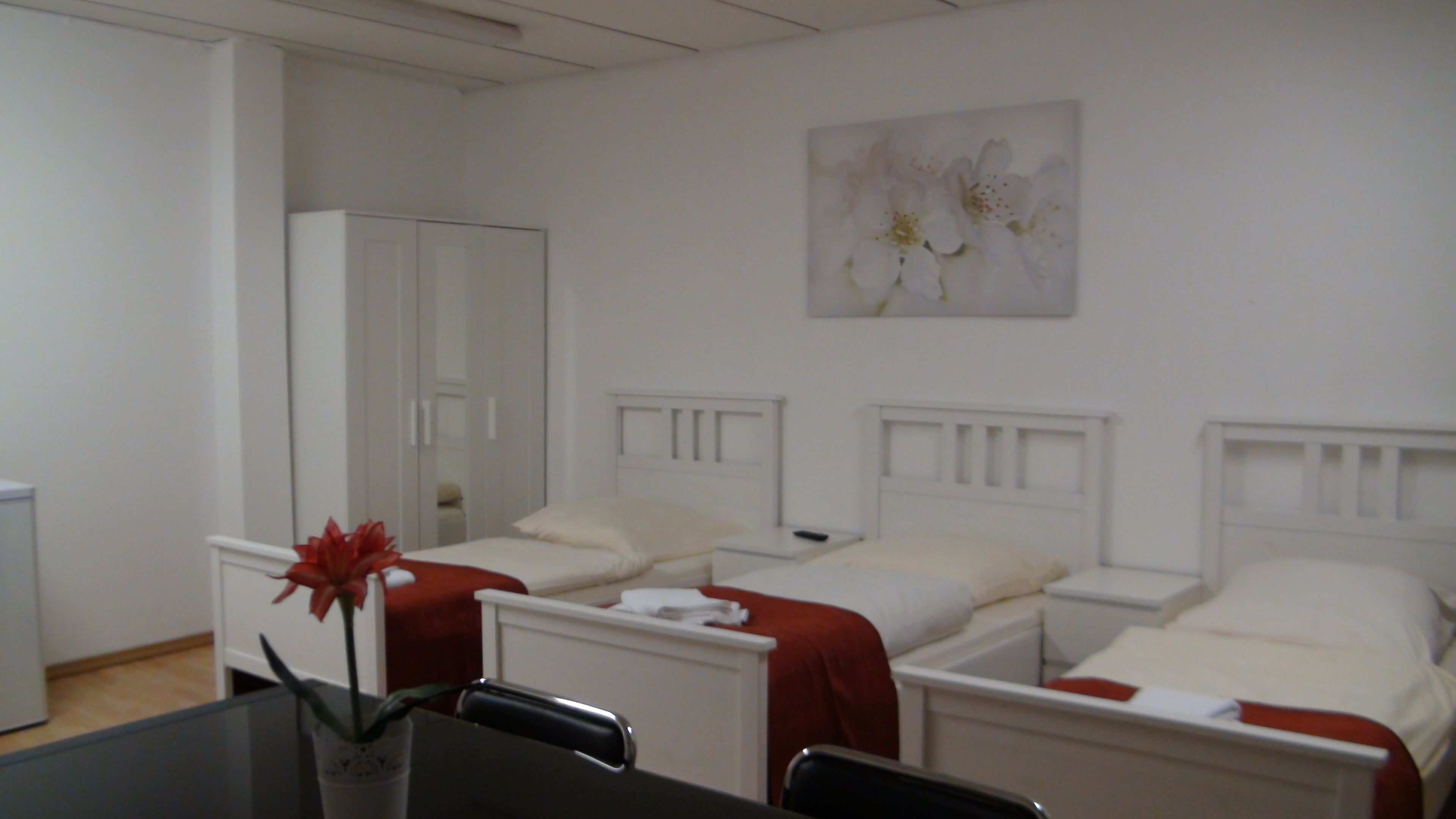 Quarto de hotel com duas camas, uma mesa, uma cadeira, um vaso com uma flor e um quadro na parede.