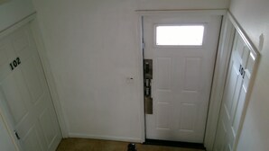 Uma porta branca com uma pequena janela, um toque e um botão de campainha.