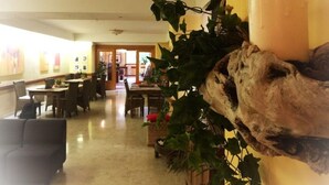 Um hall de hotel com um corredor comprido, áreas de estar e uma grande planta.