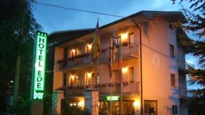Hotel com varanda no segundo andar, placa indicando um bar e várias bandeiras.