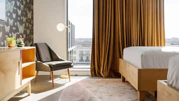 Quarto de hotel moderno com uma janela grande, uma cama, uma mesa e uma cadeira.
