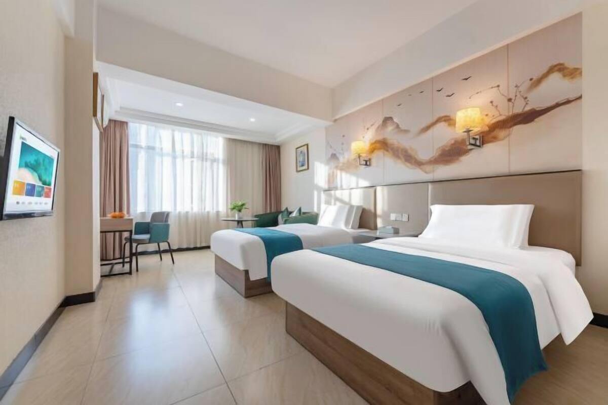 Quarto de hotel com duas camas, uma escrivaninha, uma cadeira e um mural grande na parede.