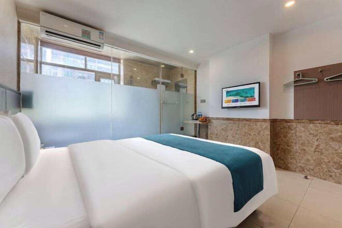 Quarto de hotel com cama, televisão, chuveiro e vista para o exterior.