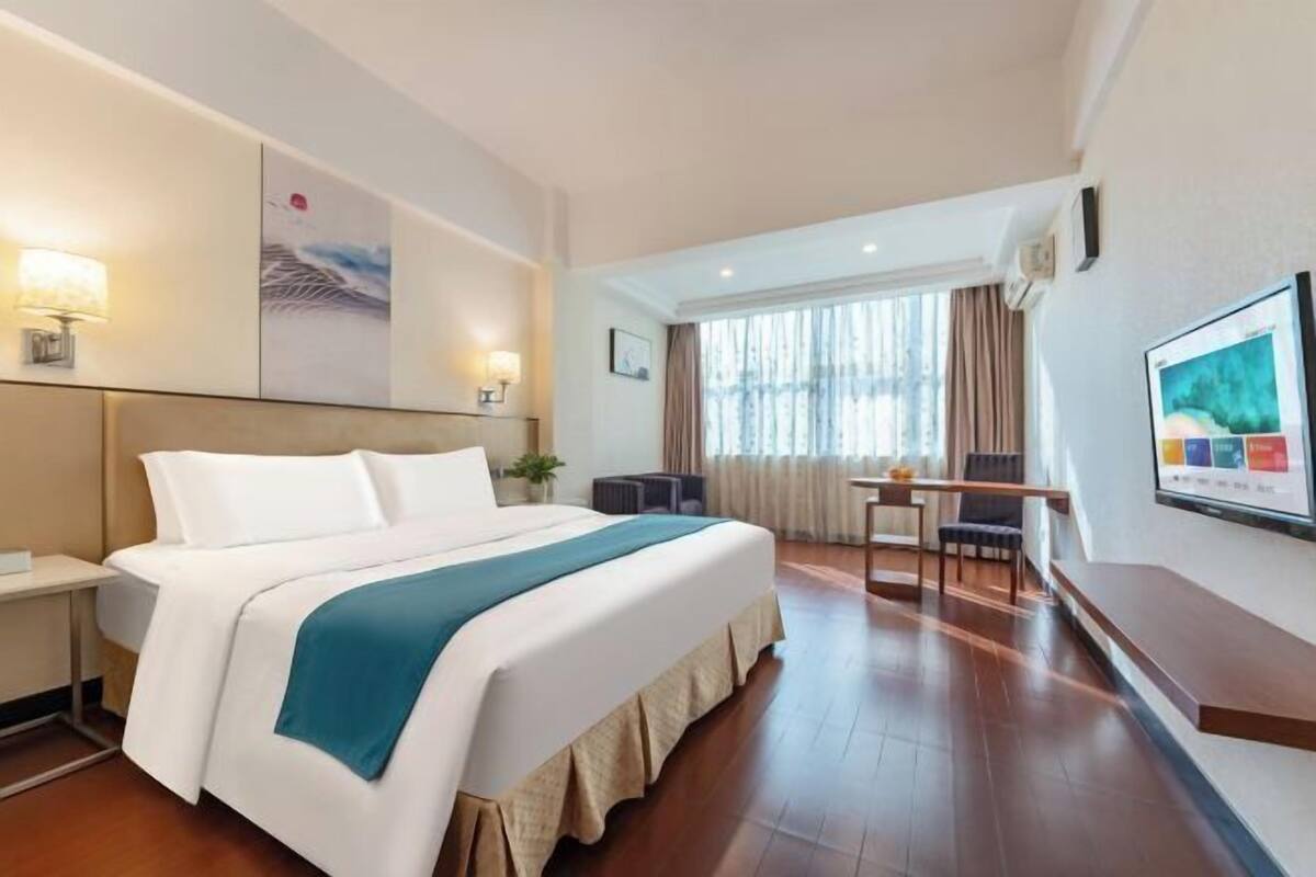 Quarto de hotel com uma cama grande, mesas de cabeceira, uma escrivaninha e uma cadeira.