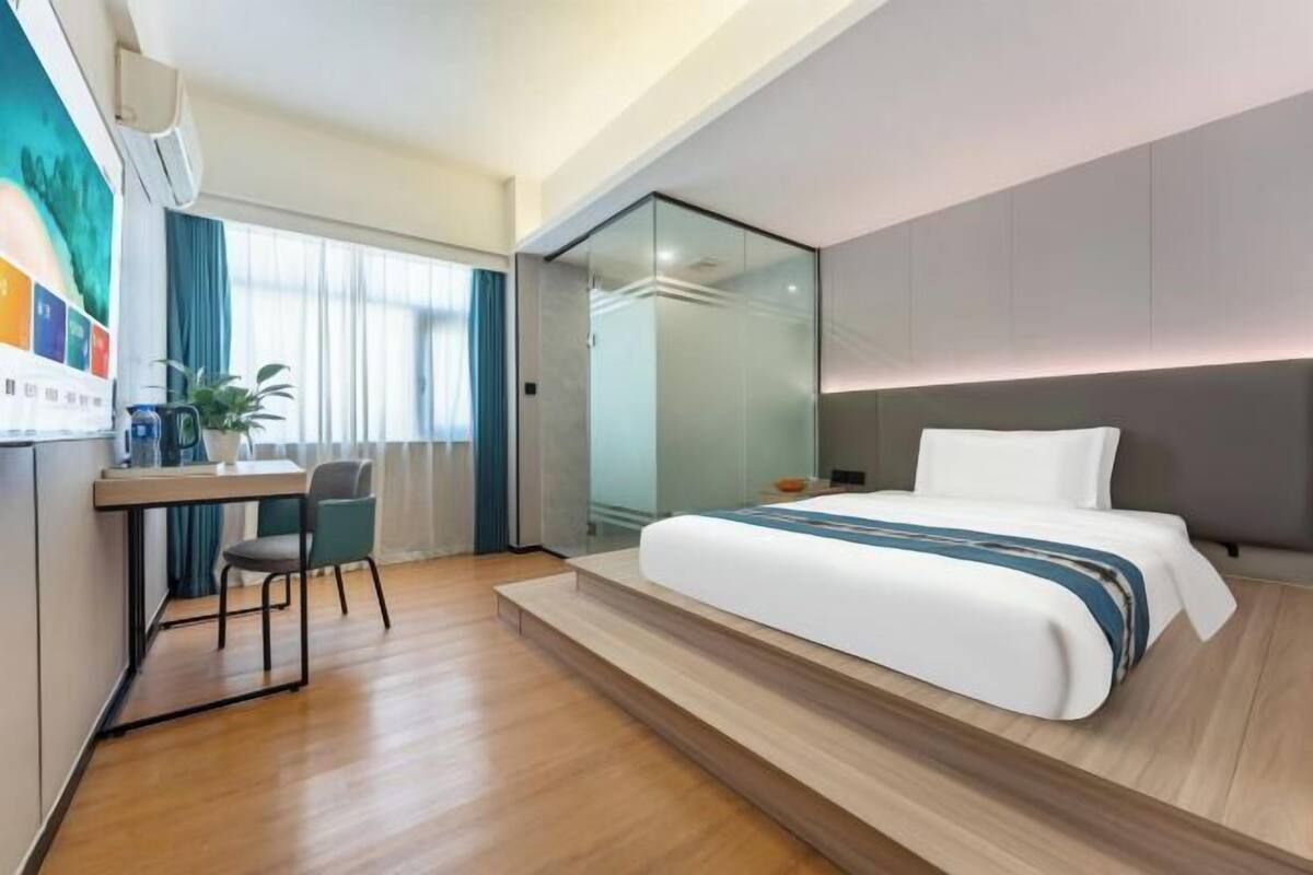 Quarto de hotel moderno com cama, escrivaninha, cadeira e divisória de vidro.