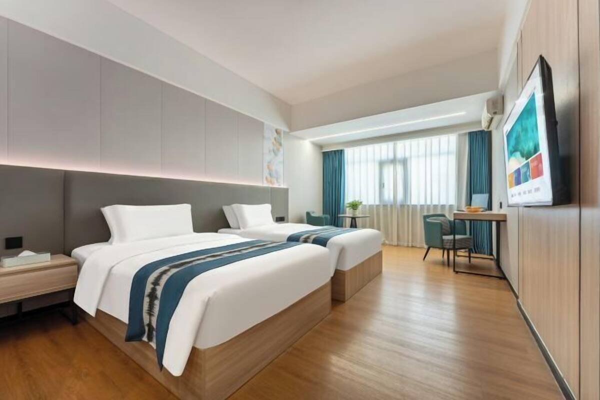Quarto de hotel com duas camas, uma mesa, uma cadeira e uma televisão.