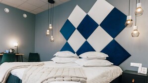 Quarto moderno com uma cama grande, várias almofadas, uma mesa de cabeceira com abajur e telefone fixado na parede.