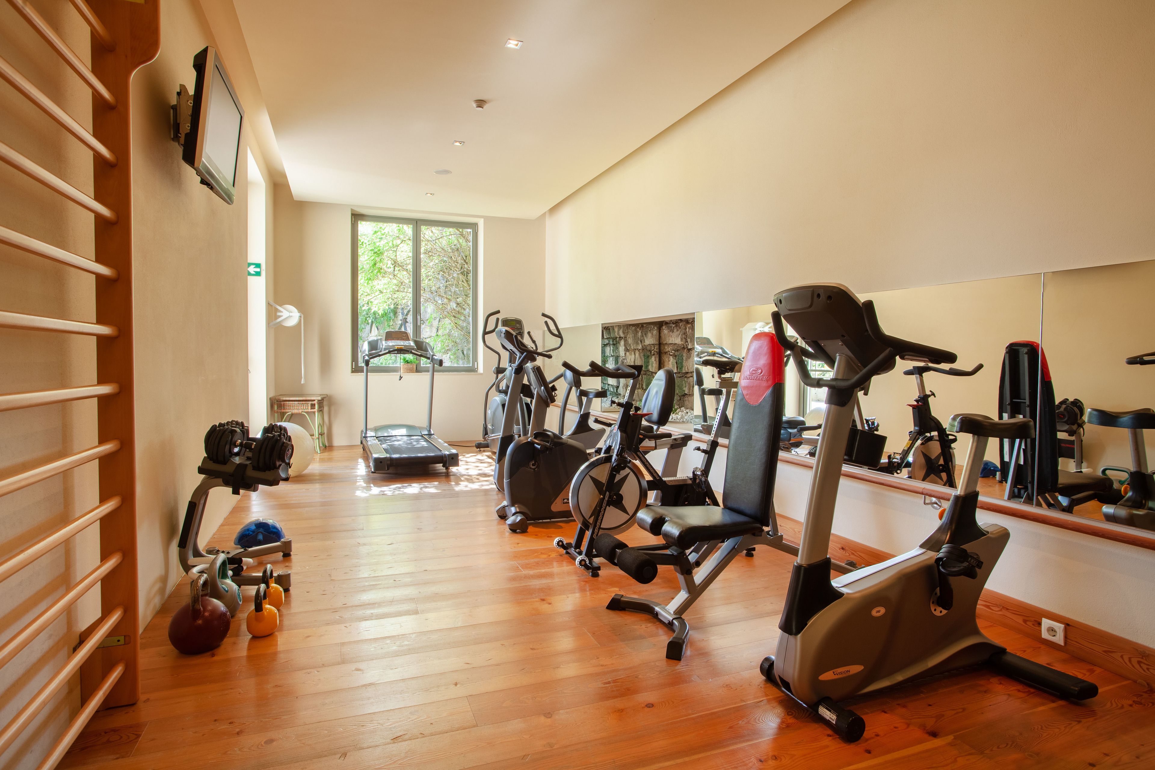 Uma academia ampla com diversos equipamentos de ginástica, um espelho grande e piso de madeira.