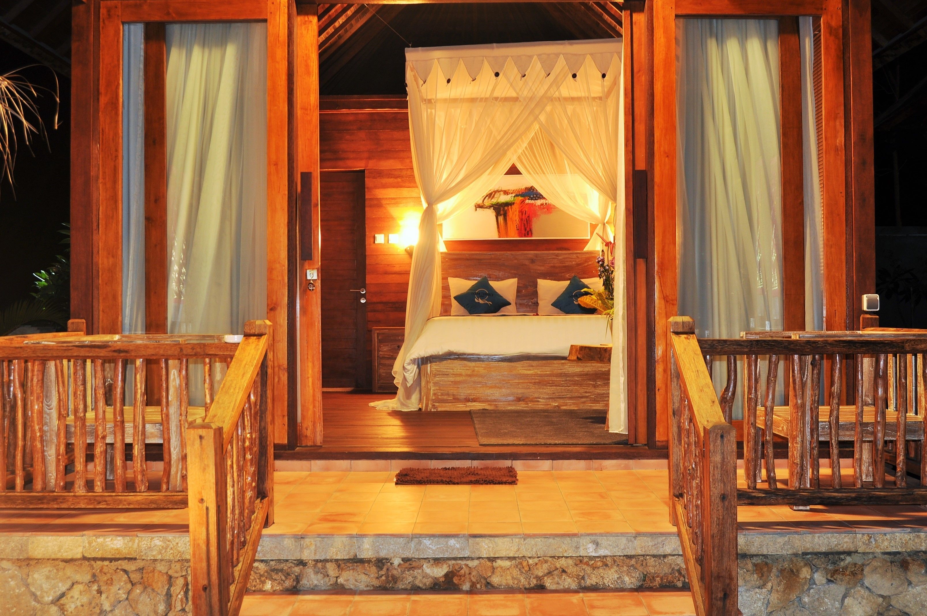 Uma cabana de madeira com cama, cortinas e uma escadaria de pedra.