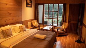 Quarto com painéis de madeira, uma cama, duas cadeiras, uma mesa e uma janela com vista para um terraço.