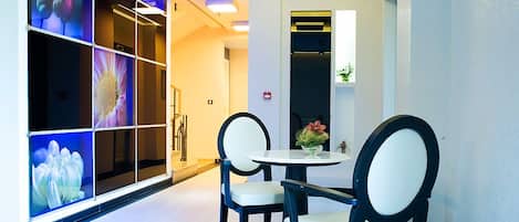 Um saguão moderno de hotel, com balcão de recepção, área de estar e painéis de vidro decorativos.